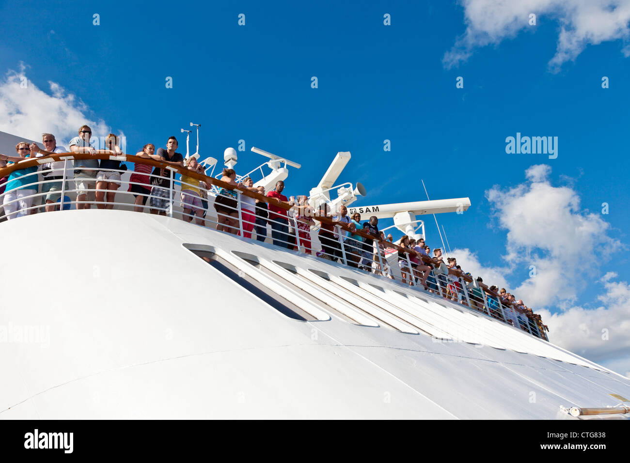 Cruise ship passengers line the rail at the bow of the ship while ...