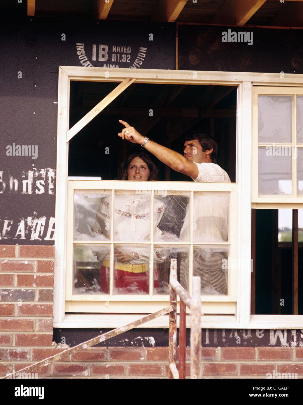 1970s COUPLE MAN WOMAN IN HOUSE UNDER CONSTRUCTION MAN POINTING OUT OF ...