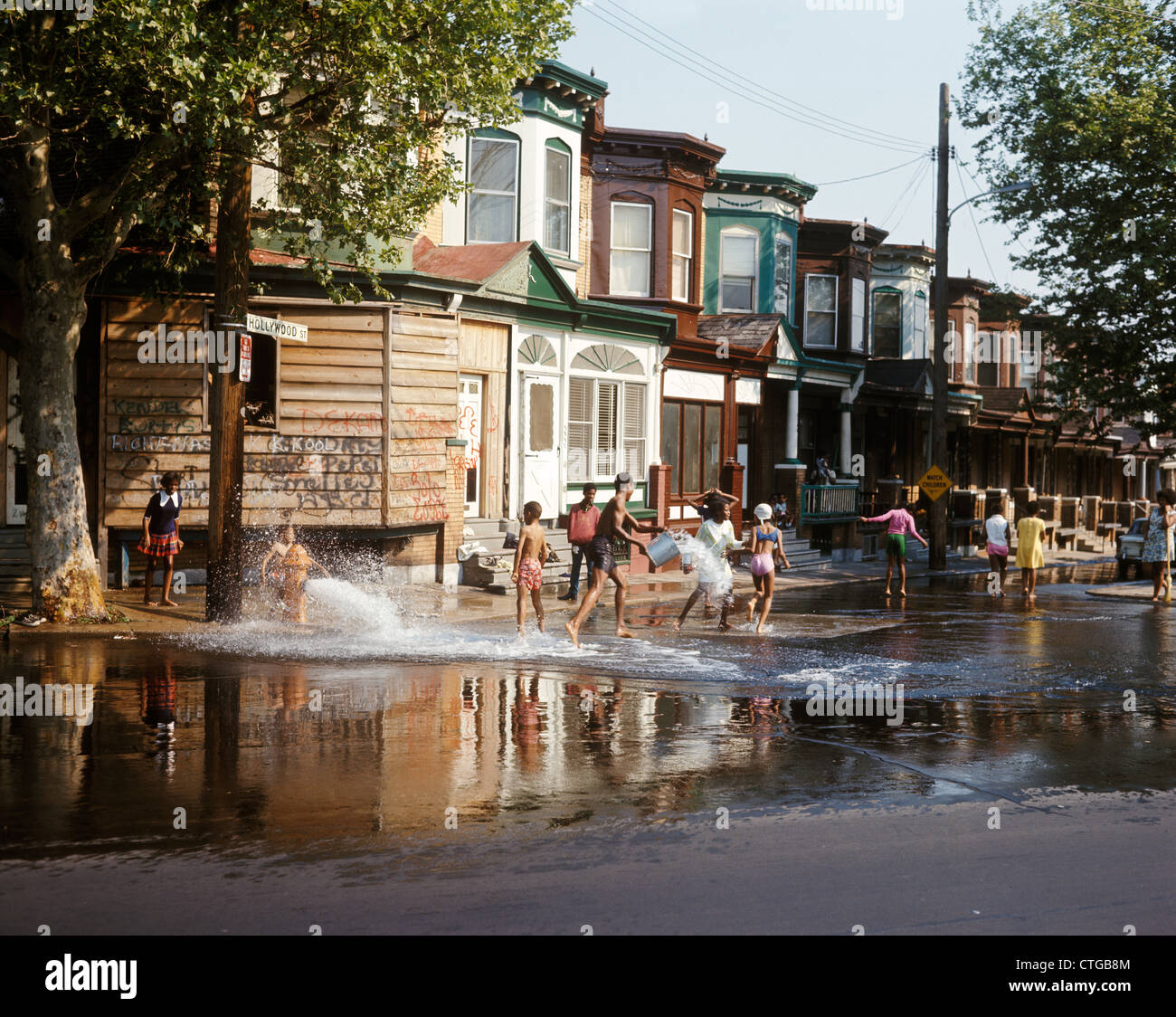 1970S CHILDREN IN CITY URBAN NEIGHBORHOOD PLAYING IN STREET IN WATER ...