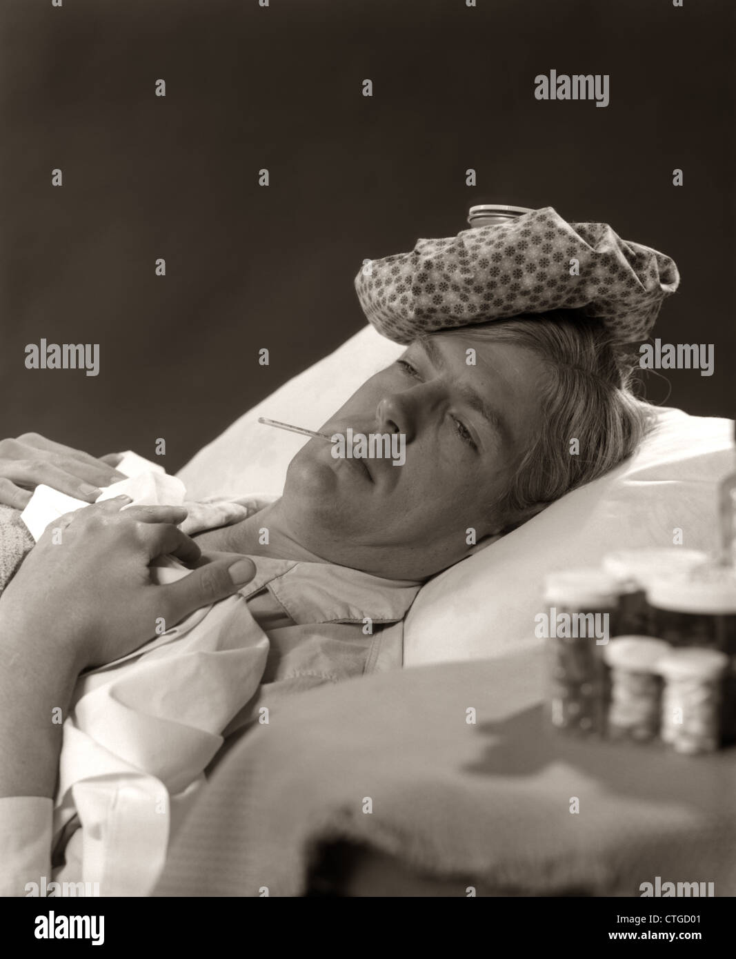 1960s 1970s MAN IN SICK IN BED WITH THERMOMETER IN MOUTH ICE PACK ON ...