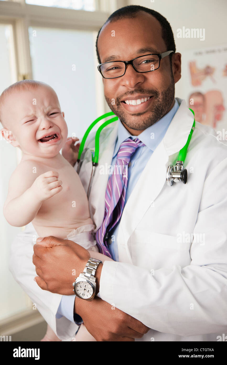 Doctor holding crying baby in doctor's office Stock Photo - Alamy
