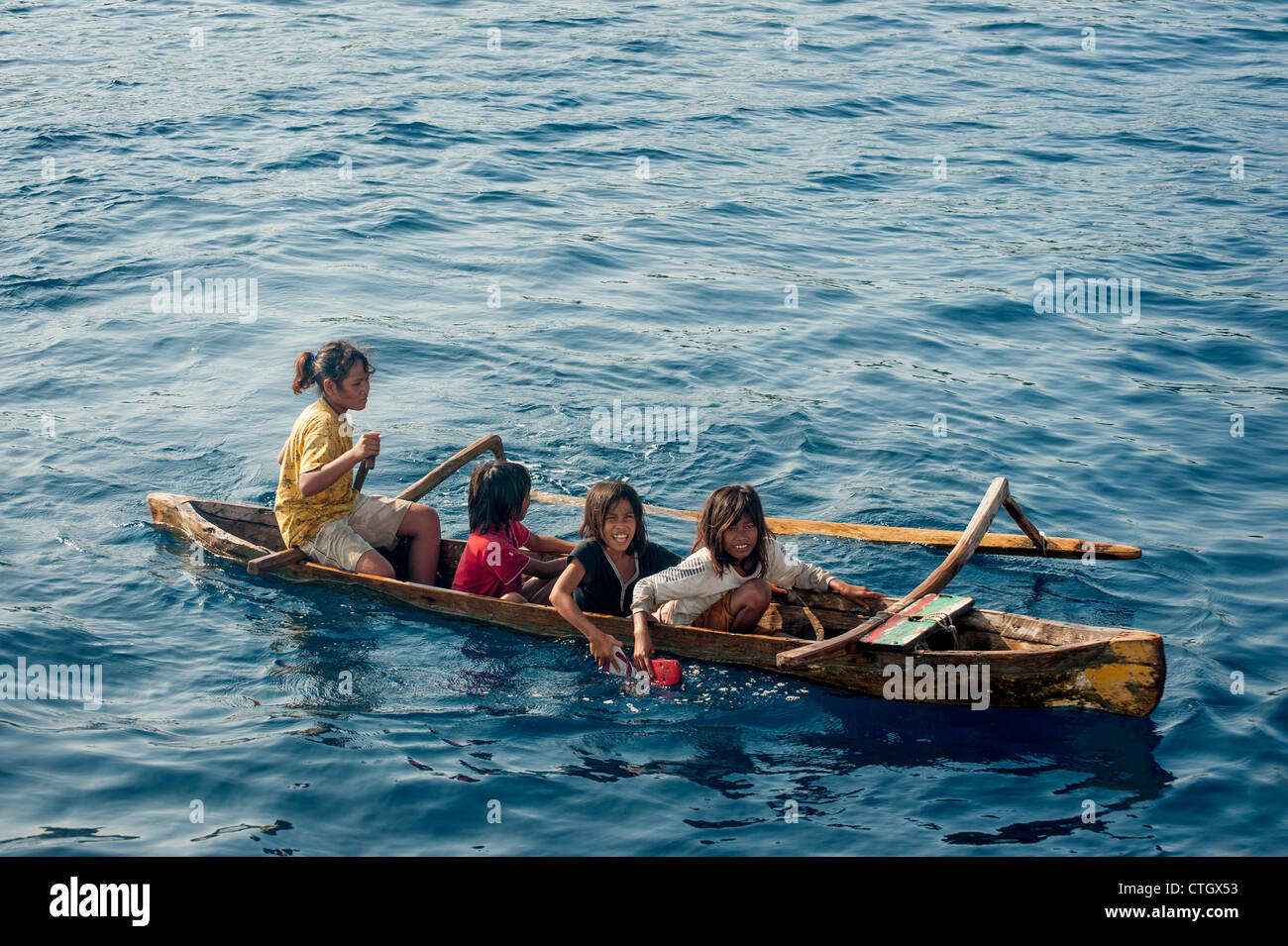 Indonesian children in a dugout outrigger canoe paddle up to seil ...