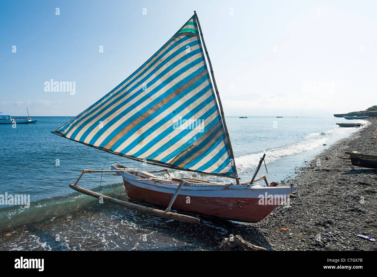 A traditional Indonesian sailing vessel pulls up to shore in the ...