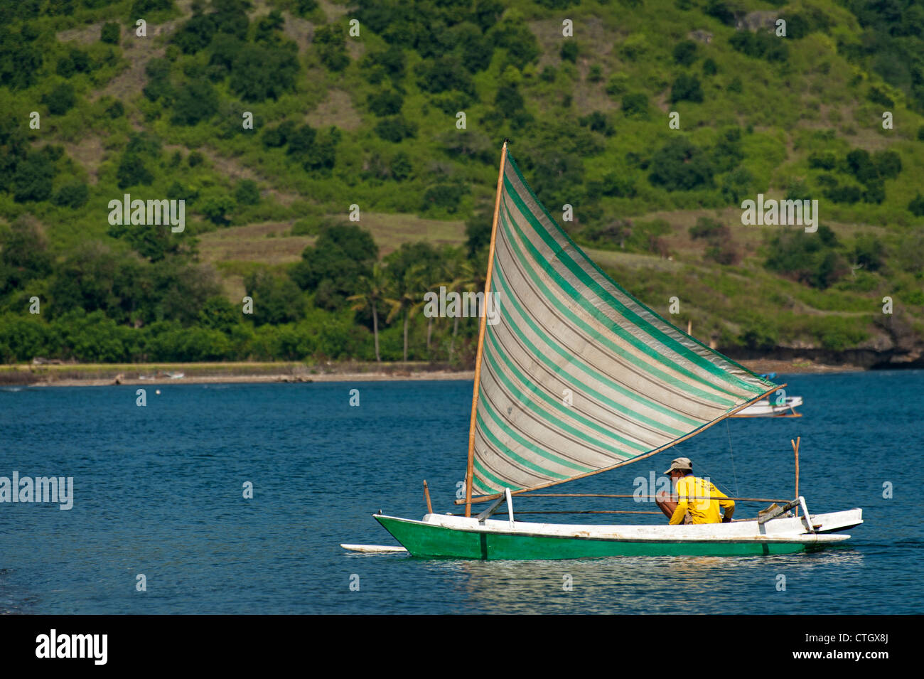 A man in a traditional Indonesian sailboat, called a jukung, off of ...