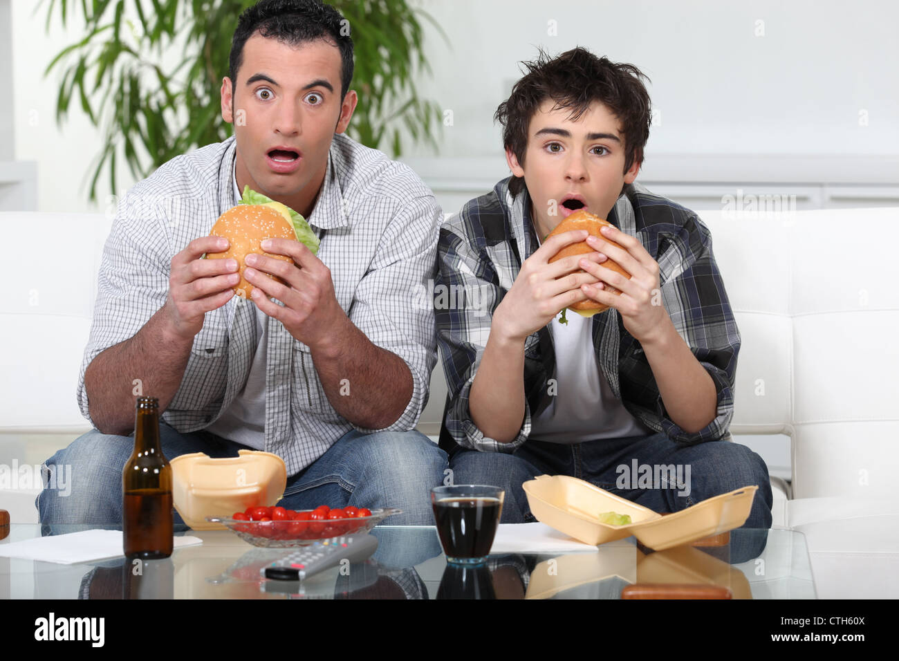 Father and son sat on the sofa eating burgers Stock Photo - Alamy