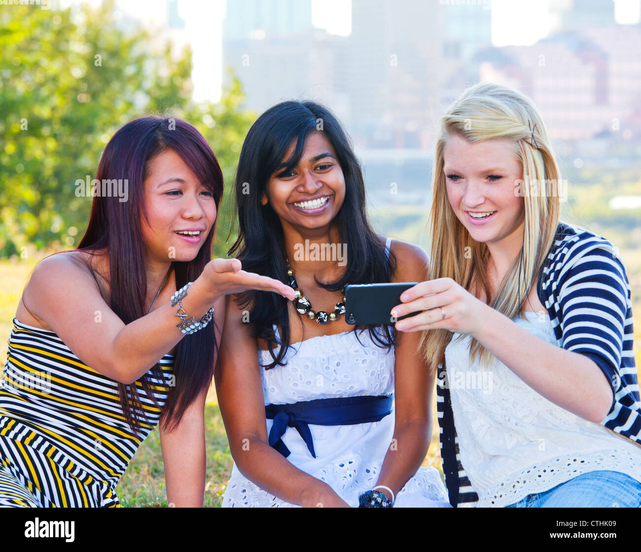 Friends Looking At A Smart Phone With A City Skyline In The Background ...