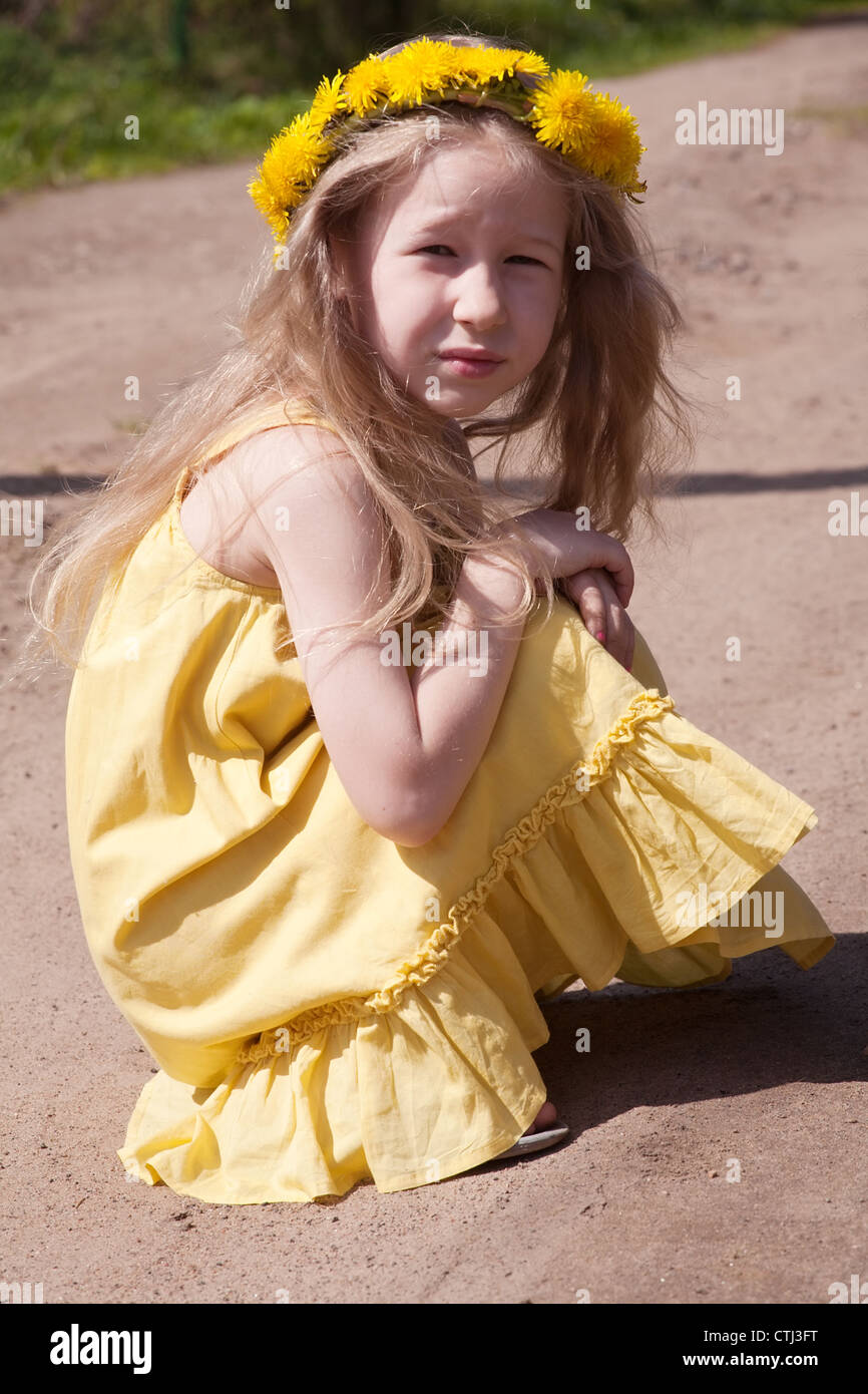 little fair-haired girl in dandelion wreath sitting in the squatting ...