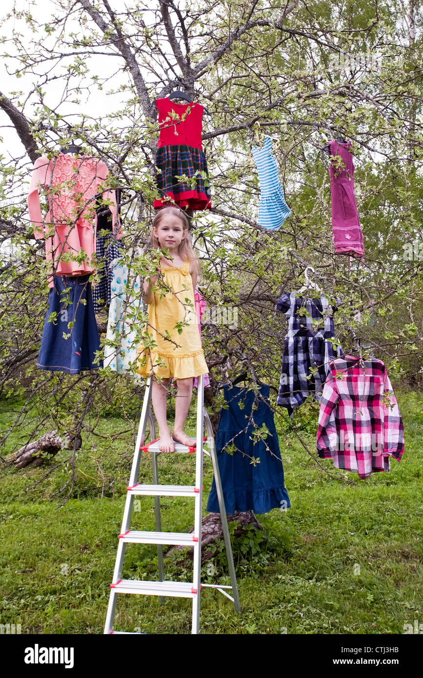 little girl standing before the tree with dresses hanging on branches ...