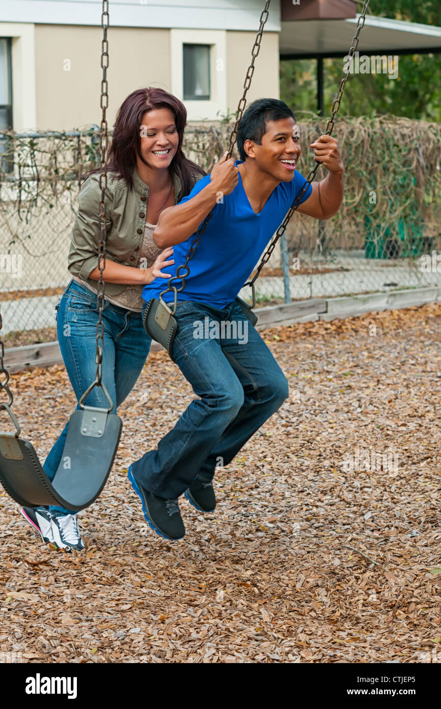 Young ethnic couple. Woman pushing man on swing enjoying a fun day at ...