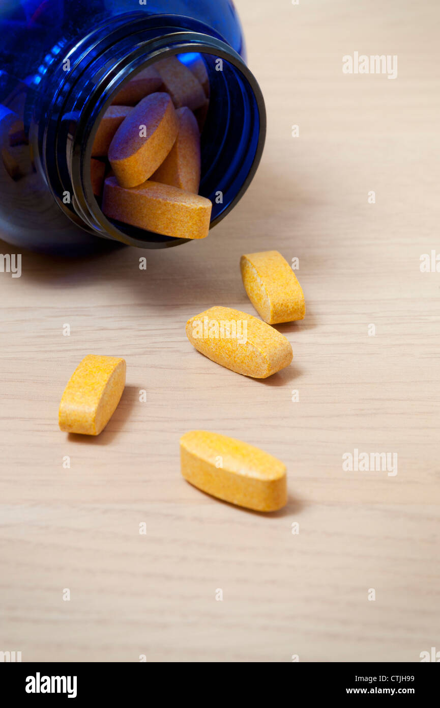 Blue bottle of yellow vitamin pills with some spilling out onto the ...