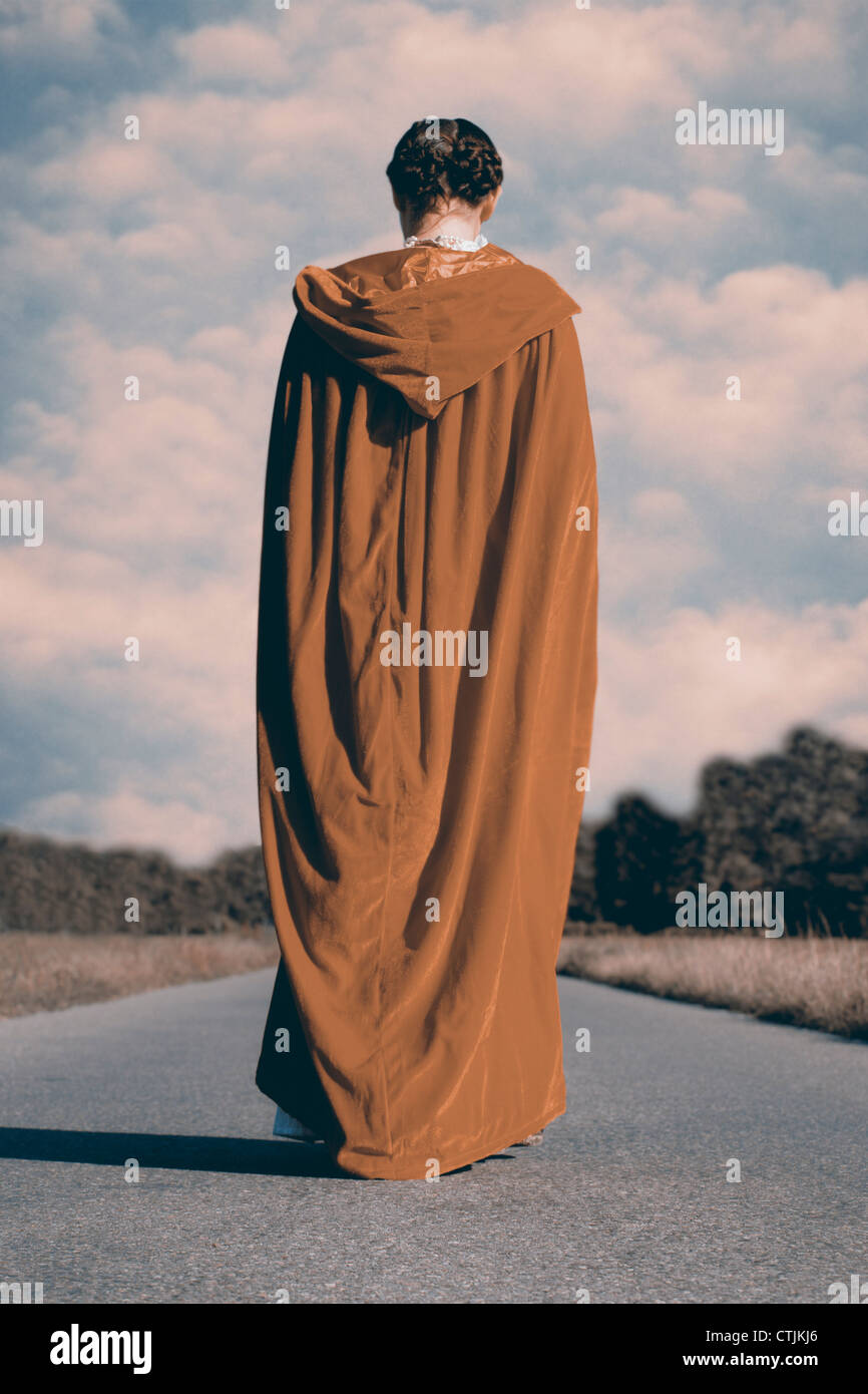 a woman in a red cape is walking along a road Stock Photo - Alamy