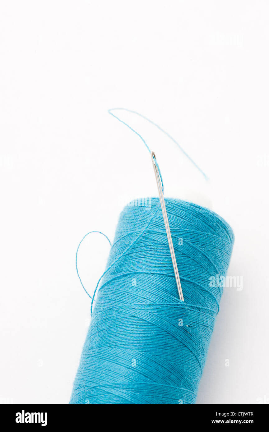 Threaded needle and spool of bright blue sewing thread Stock Photo - Alamy