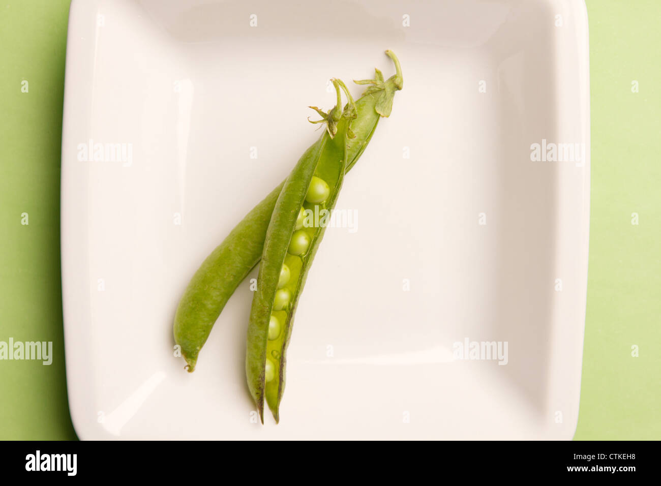 Two open pea pods on a white plate, placed on a bright green background ...