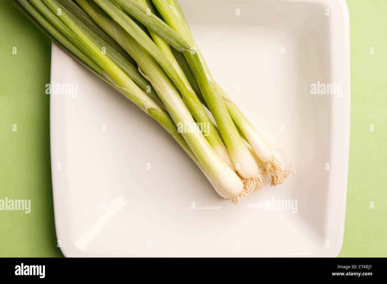 A handful of spring onions on a white plate, placed on a bright green ...