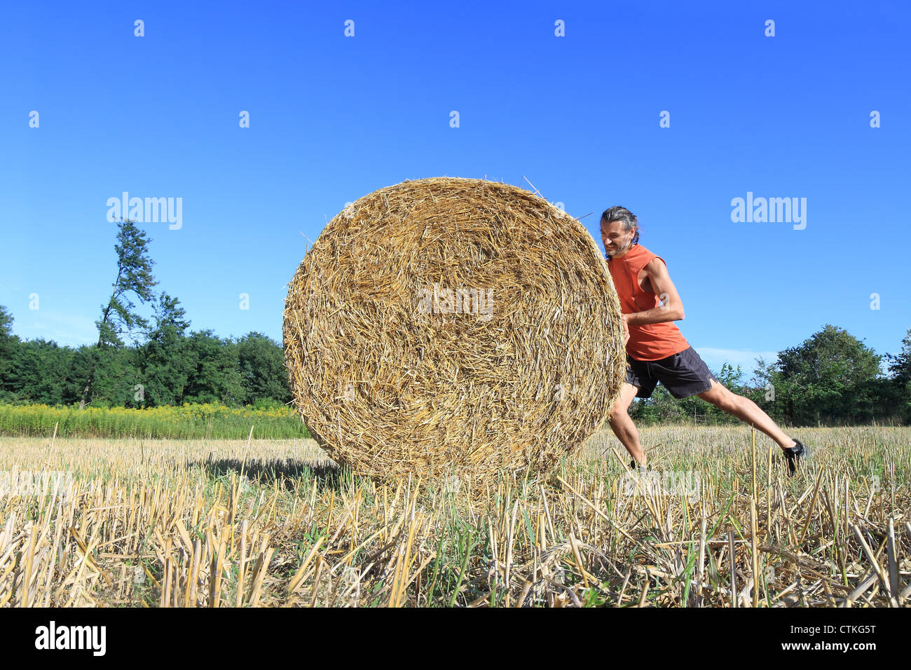 Effort concept, sporty man pushing a hay bale Stock Photo - Alamy