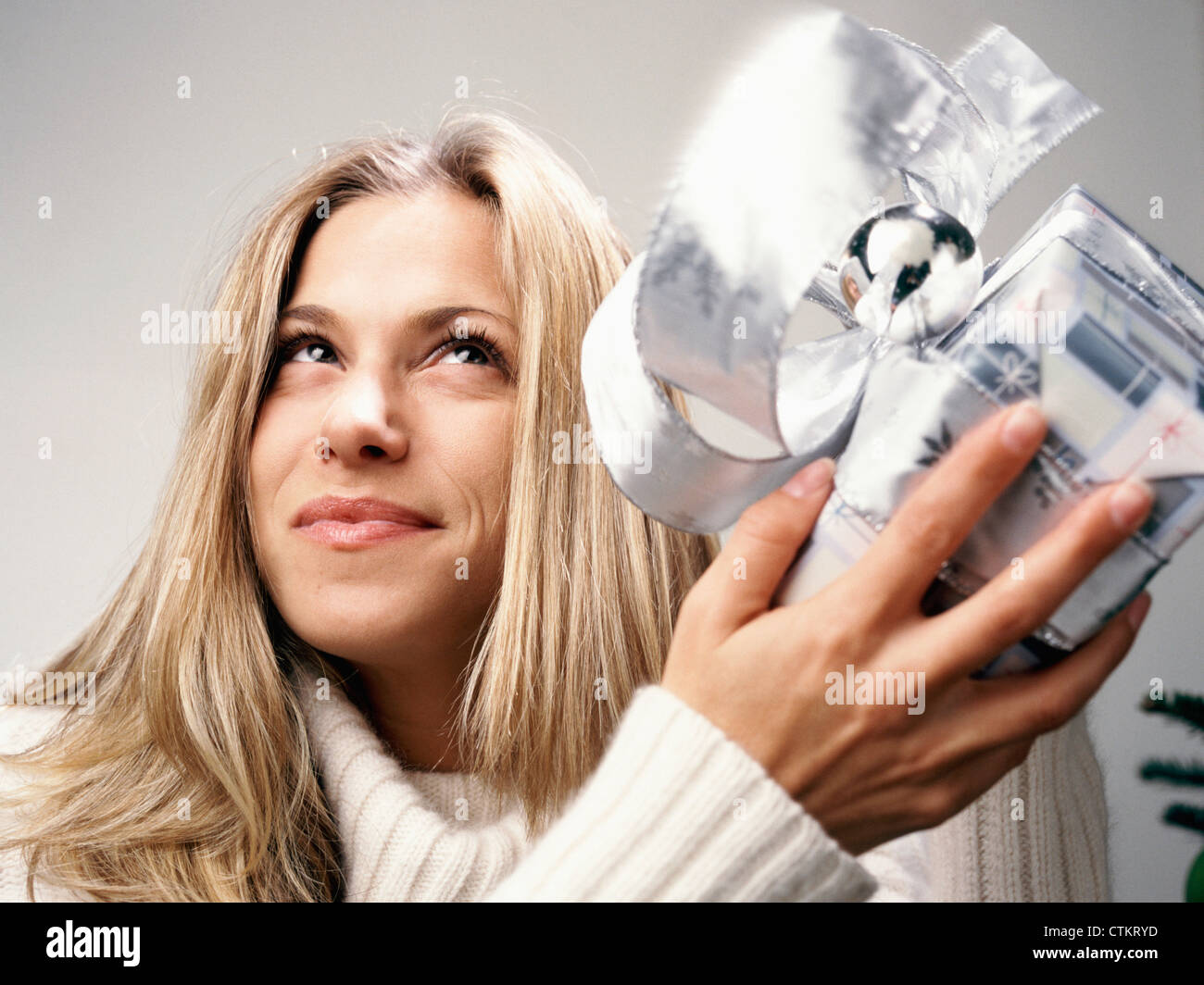 A woman in her 20's-30's shaking a present and listening to what's ...