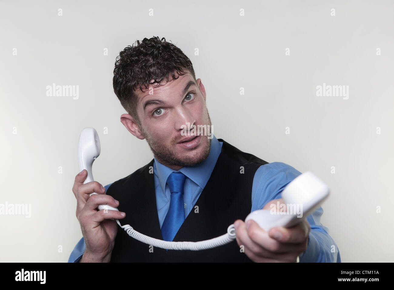 handsome man holding up two phones connected by a single telephone wire ...