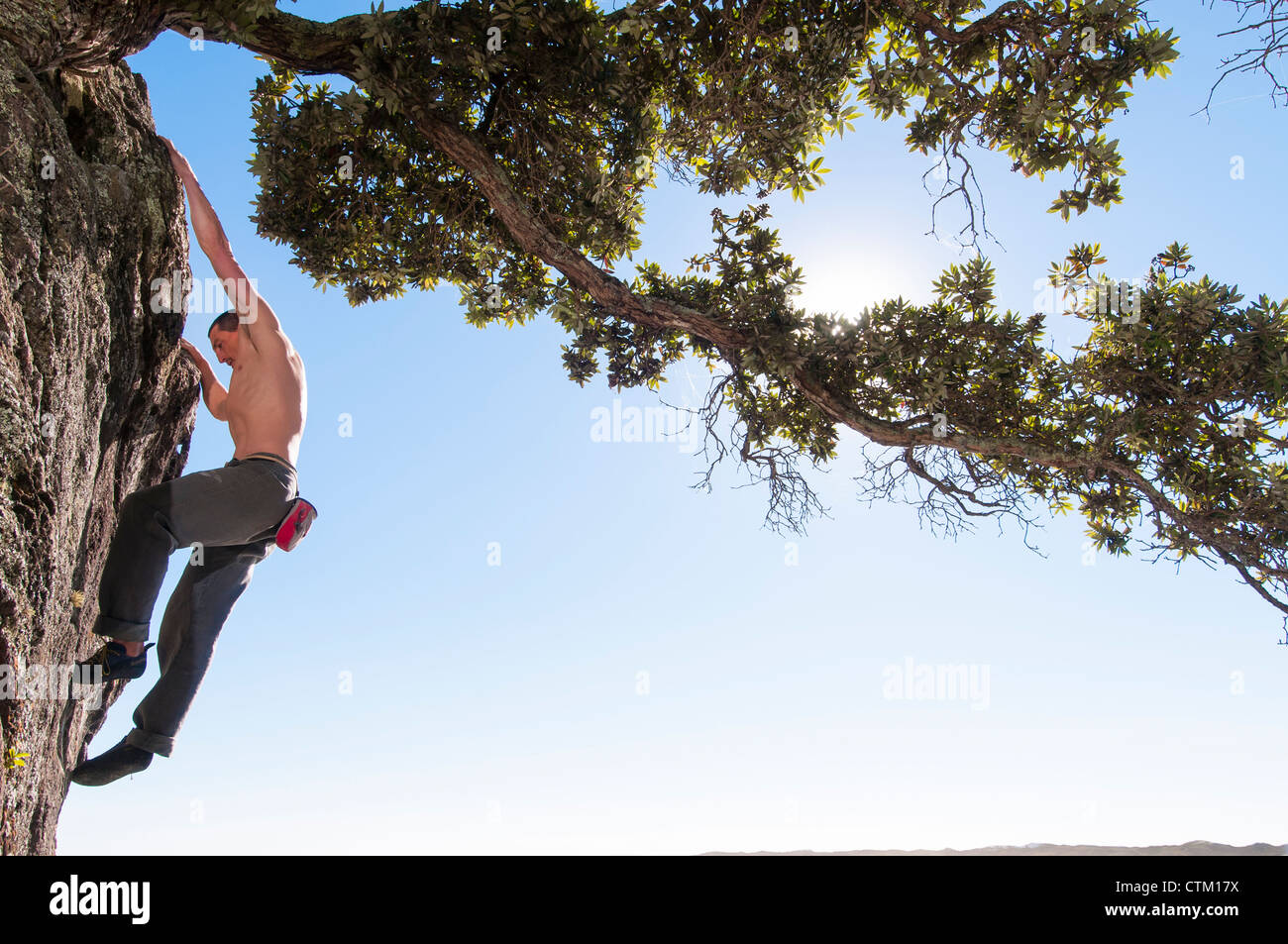 Man climbing cliff face, with ocean and rocks underneath, Raglan , New ...