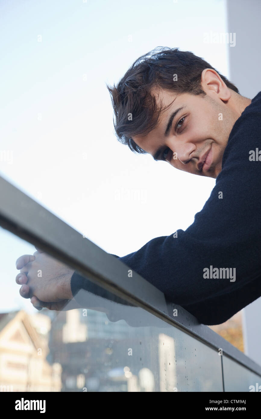 Portrait of a handsome young man leaning on glass railing of a balcony ...