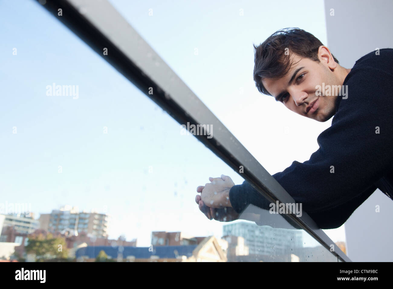Portrait of a handsome young man leaning on glass railing of a balcony ...
