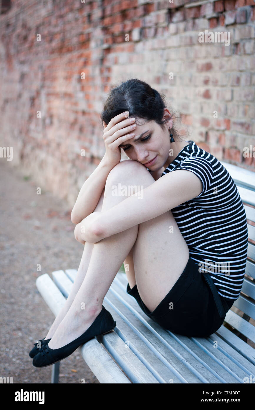 Depressed young woman sitting on a bench in an urban area Stock Photo ...