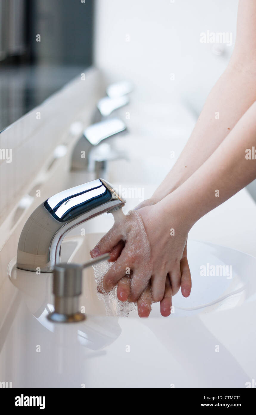 Washing hands in a public restroom (focus on the tap, hands in motion ...