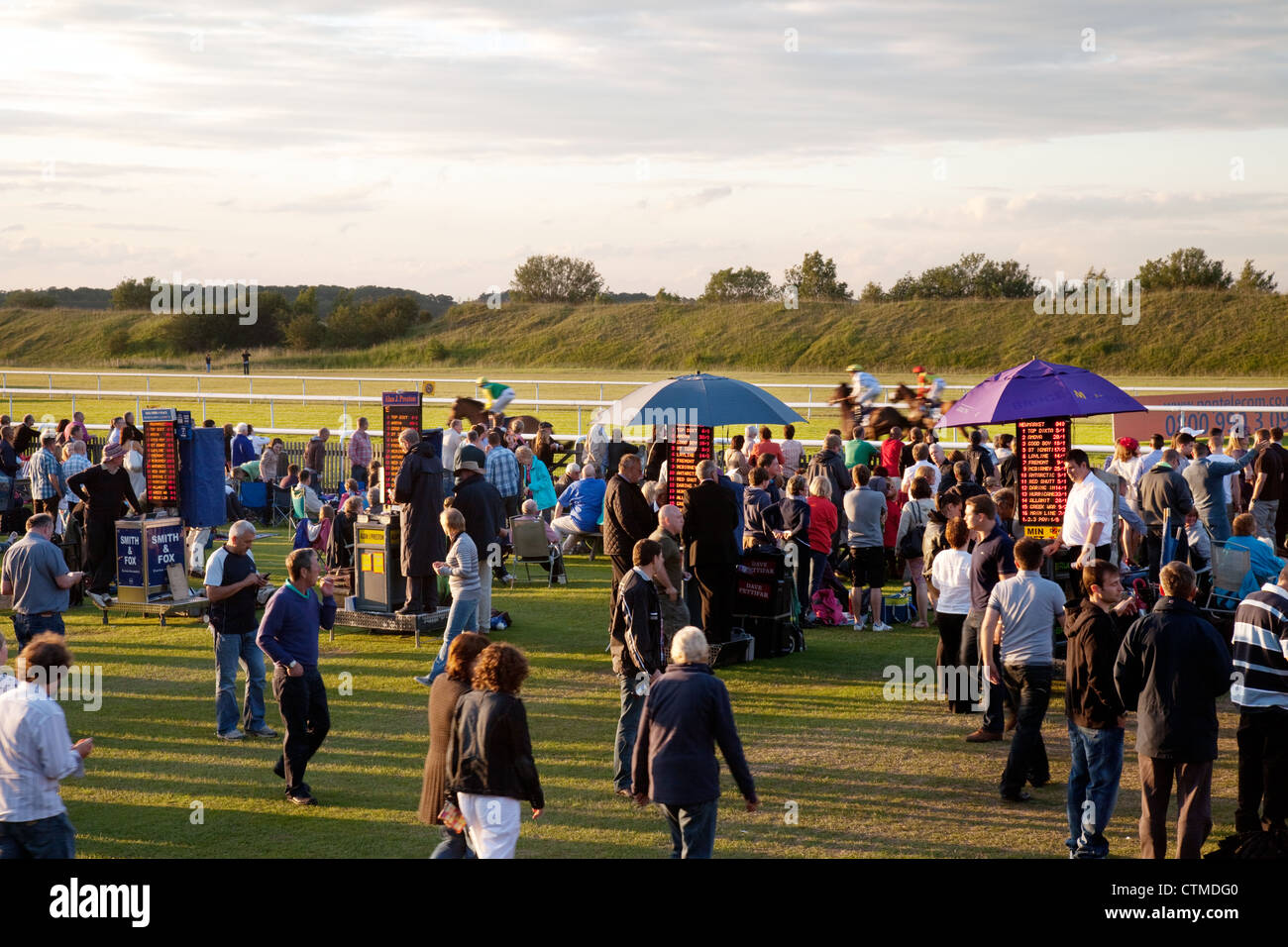 people watching the horse racing at an evening meeting July racecourse ...