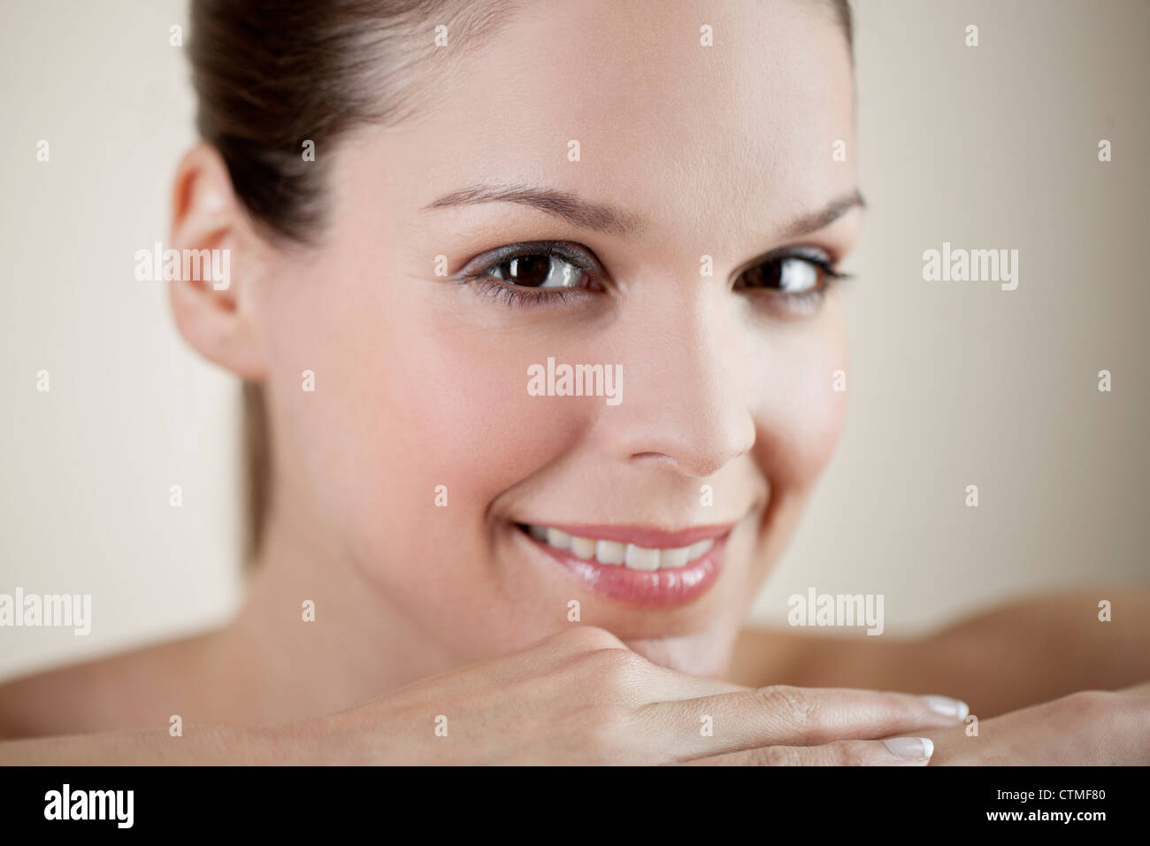 A young brunette woman smiling to camera, head resting arms, close-up ...