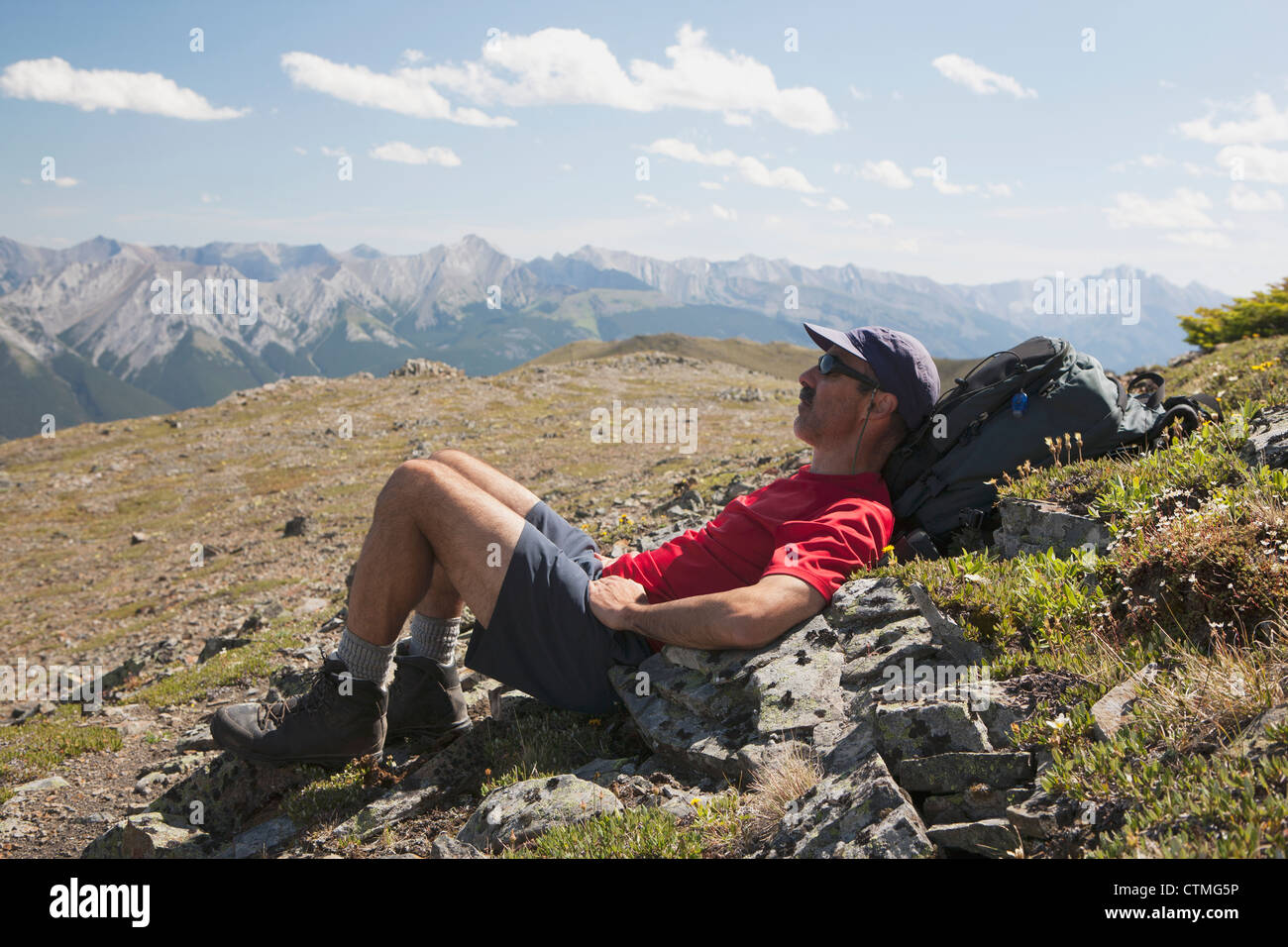 Male Hiker Laying In Meadow With Mountain Range In The Distance And ...
