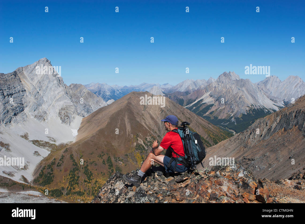 Male Hiker Sitting On Top Of Mountain Ridge Overlooking Valley And ...