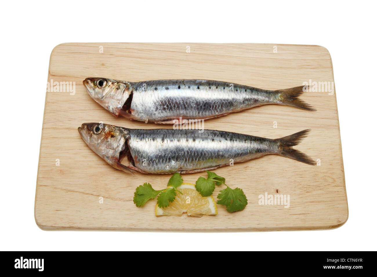 Two fresh sardines on a wooden food preparation board with lemon and ...