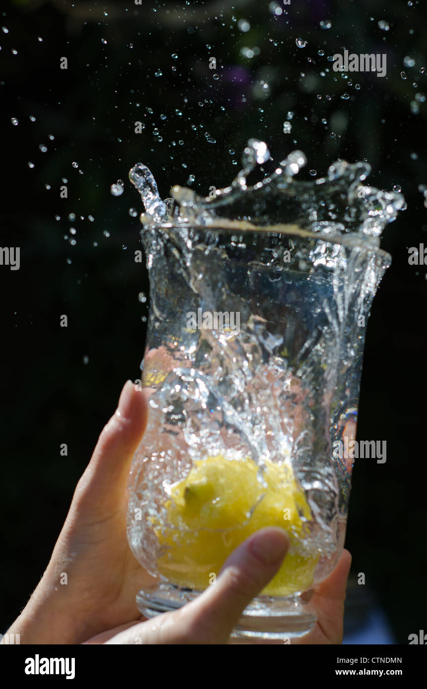Water pouring and splahing into glass jug filled with lemons on sunny ...