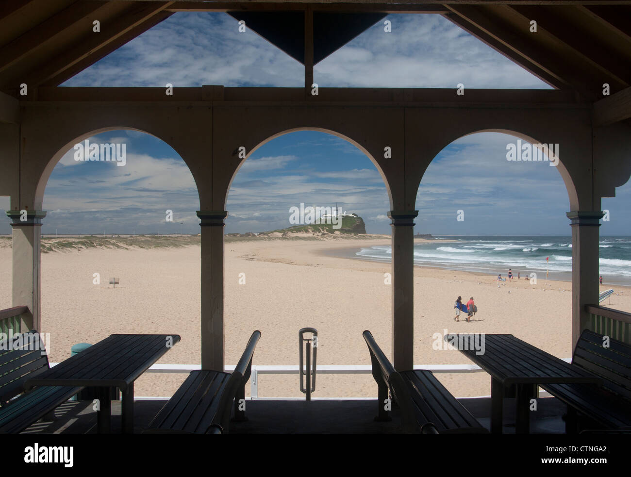 Nobbys Beach and headland seen through arches of cafe with two surfers ...