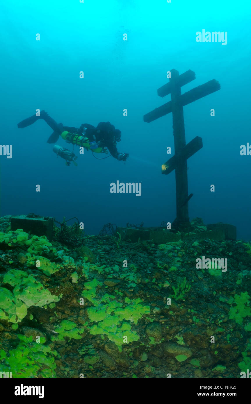 Scuba diver looks at a large cross mounted on an underwater rock in ...