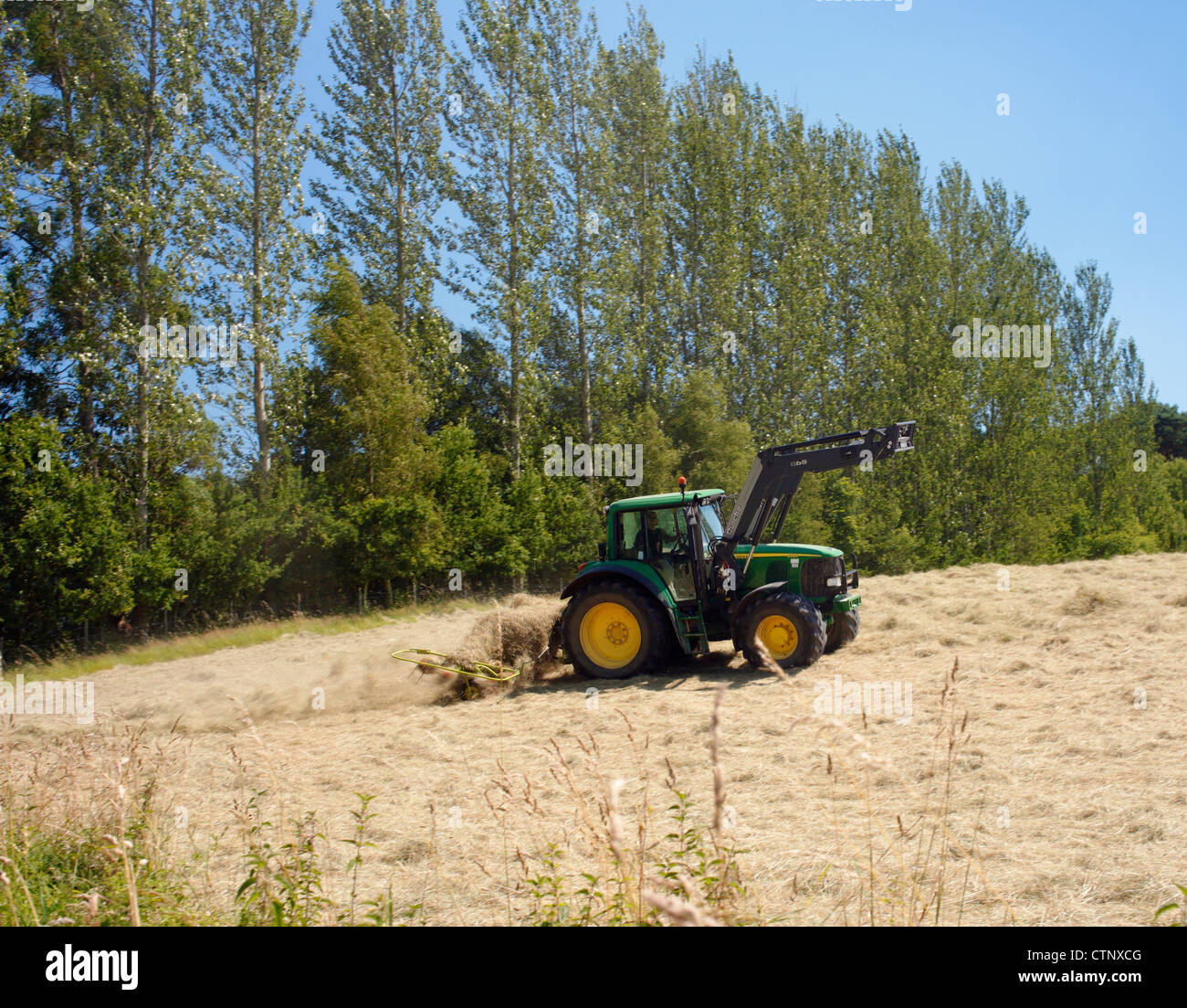 Tractor turning hay with a Hay bob Stock Photo - Alamy