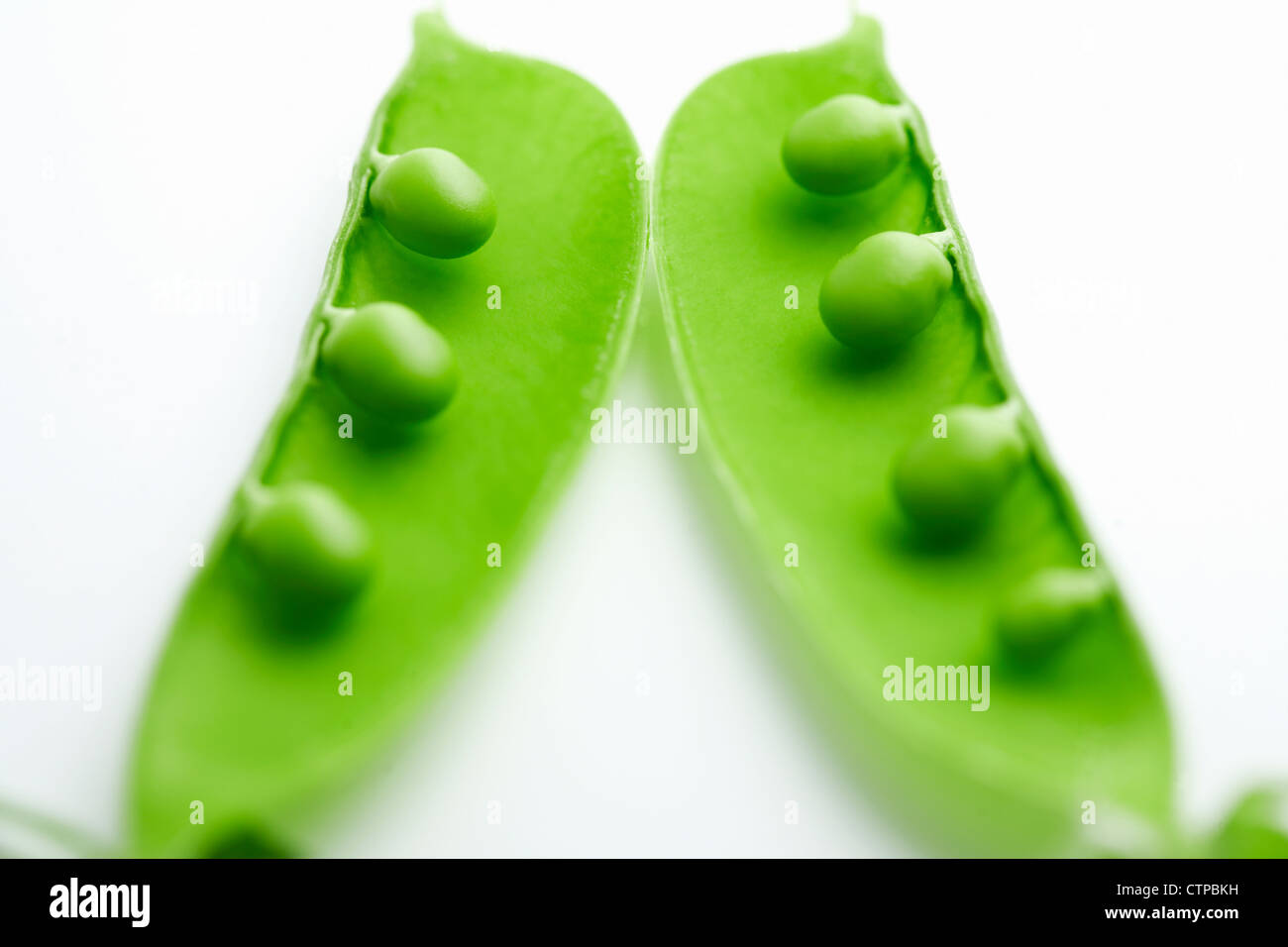 A close-up of a pea pod split open revealing peas on white background ...