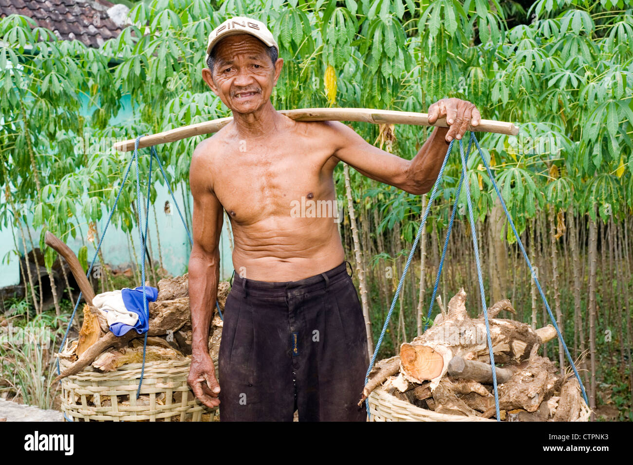 local villager in rural village street with wood filled baskets hanging ...