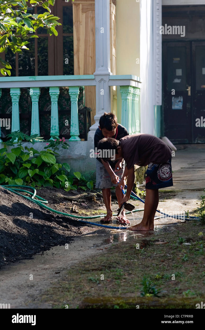 two village children wash their feet with a hosepipe in the garden of ...
