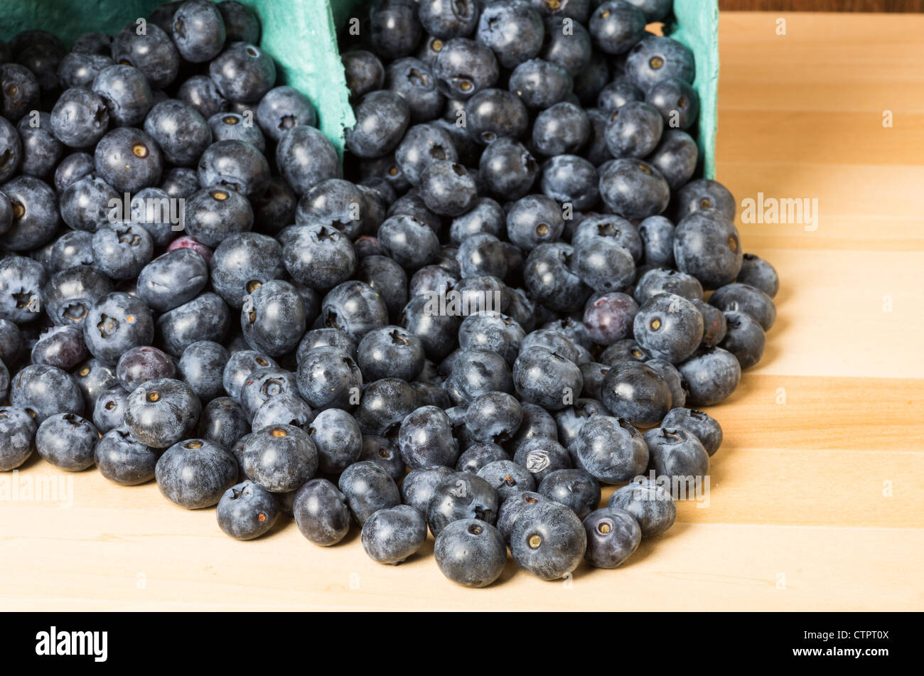 Blueberies spilling onto wooden table with green container Stock Photo ...