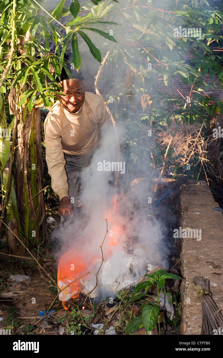local man burning household rubbish on waste ground in small village ...