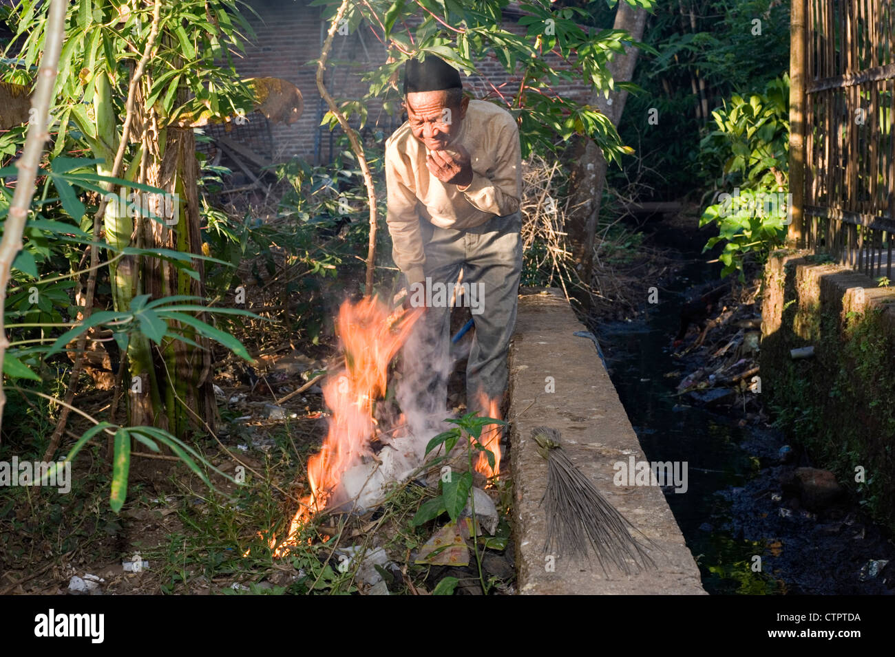 local man burning household rubbish on waste ground in small village ...