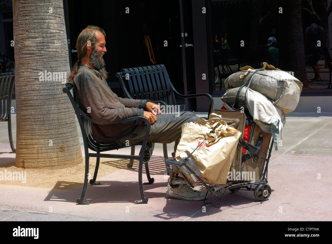 A homeless male adult in his thirties sits on a public bench outside at ...