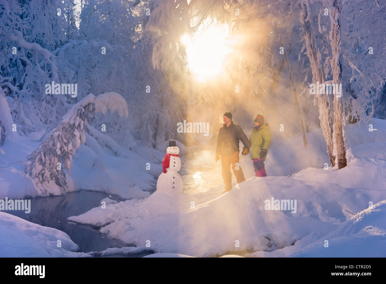 Husband wife standing in frosty forest next to snowman backlit by ...
