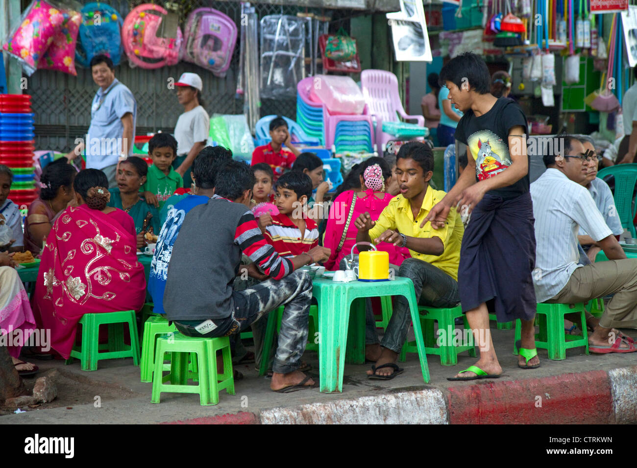 Burmese people eat and drink at small tables and chairs outdoors in ...