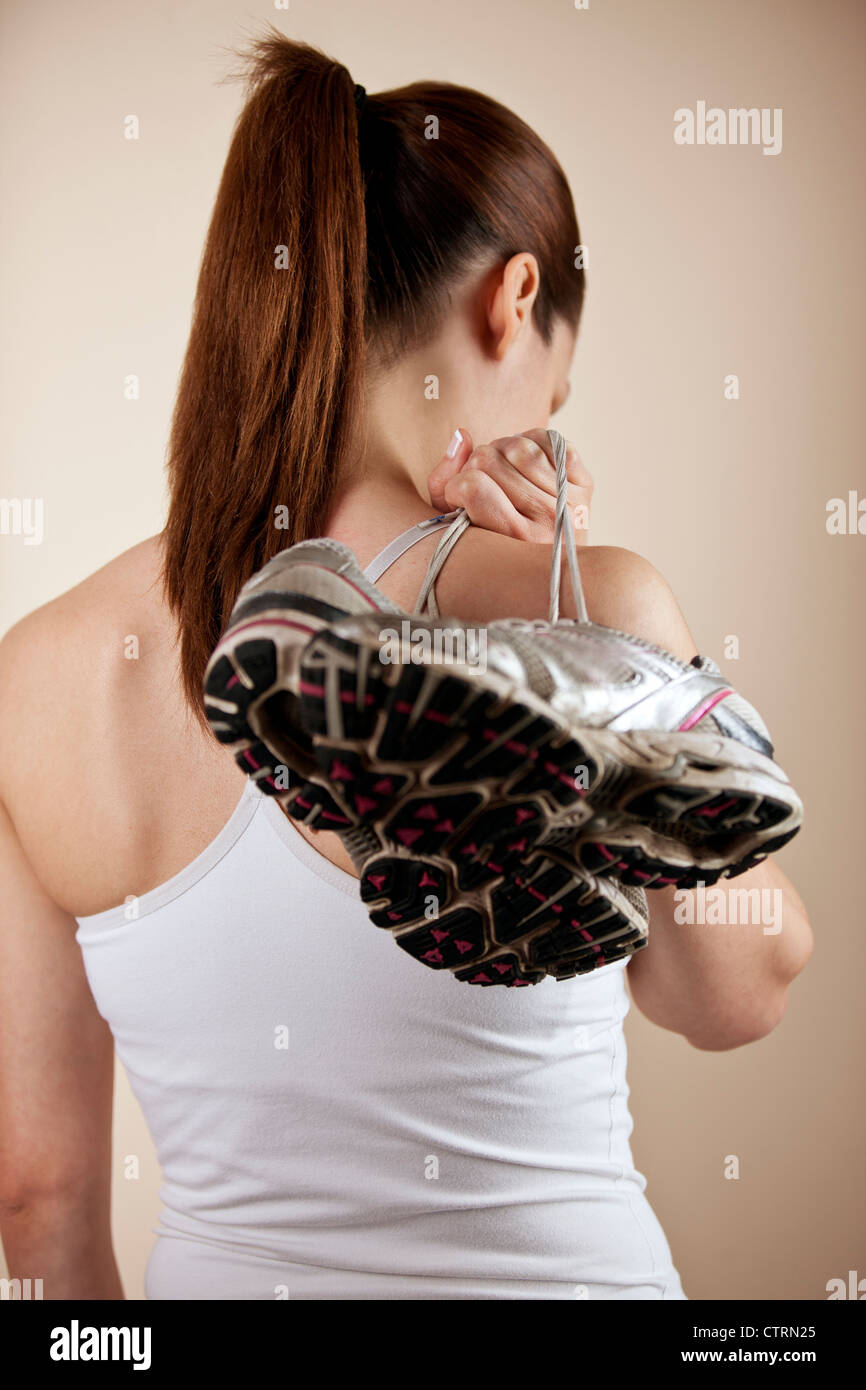 A young woman carrying a pair of training shoes over her shoulder ...
