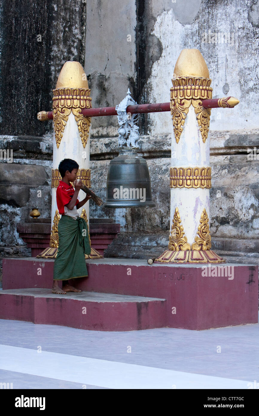 Myanmar, Burma, Bagan. Young Boy Striking Temple Bell. He is wearing a ...