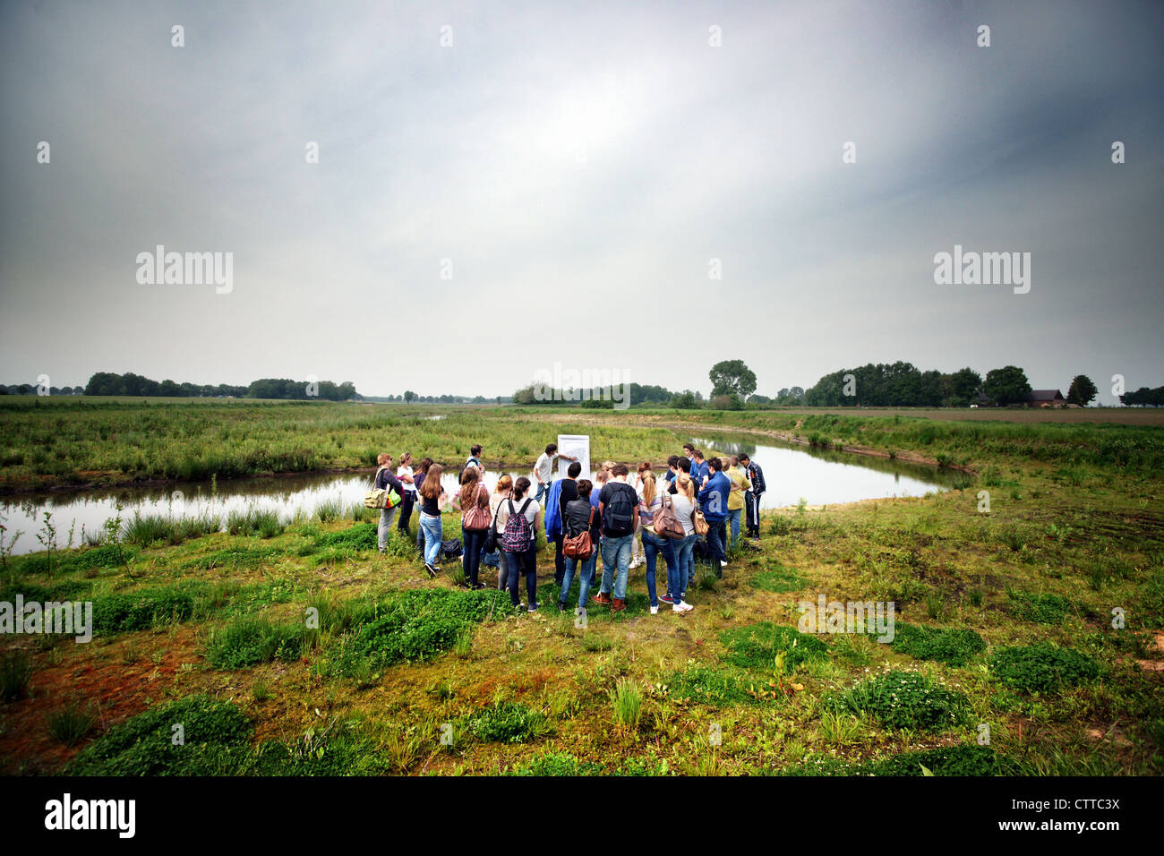 a group of young students on a excursion in the field next to a creek ...