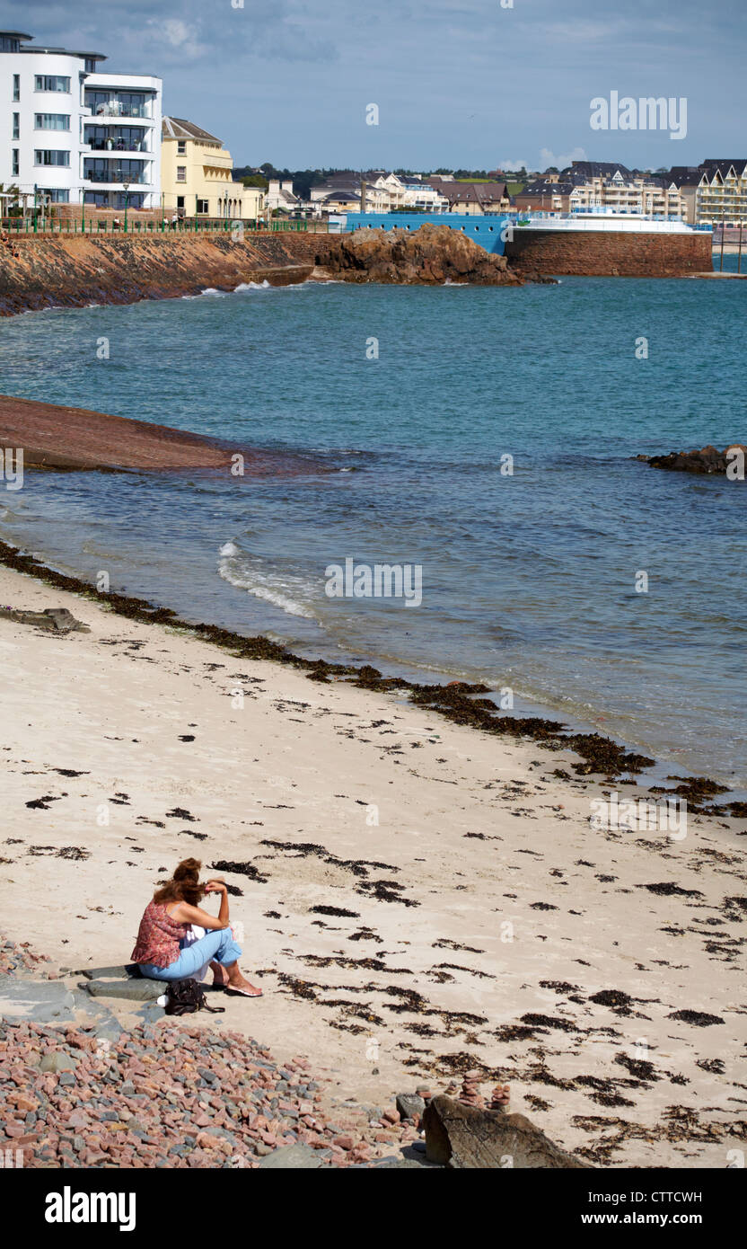 Young woman sitting on rock on beach at St Helier, Jersey in July Stock ...