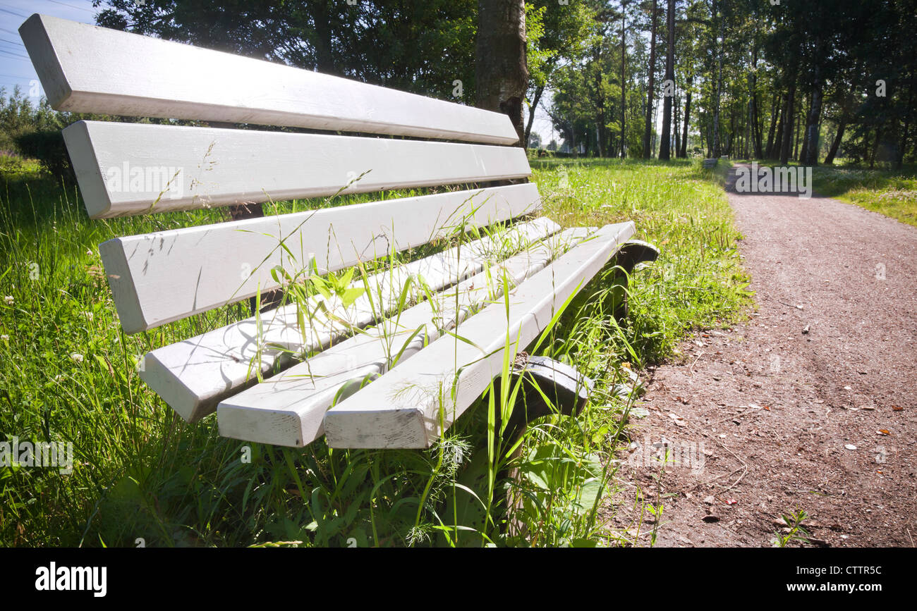 White park bench with grass growing through Stock Photo - Alamy