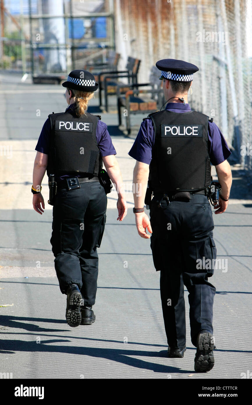 British Police Man and Woman patrol a footpath around a fenced ...